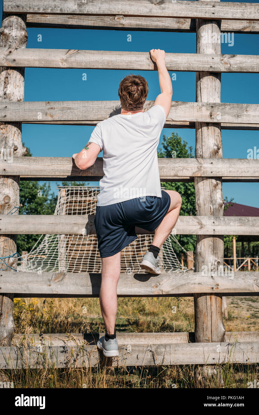 back view of soldier climbing wooden barrier during obstacle run on ...