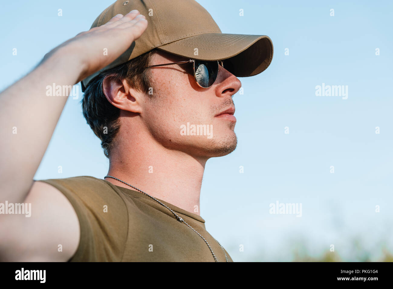 side view of young soldier in cap and sunglasses against blue sky Stock ...
