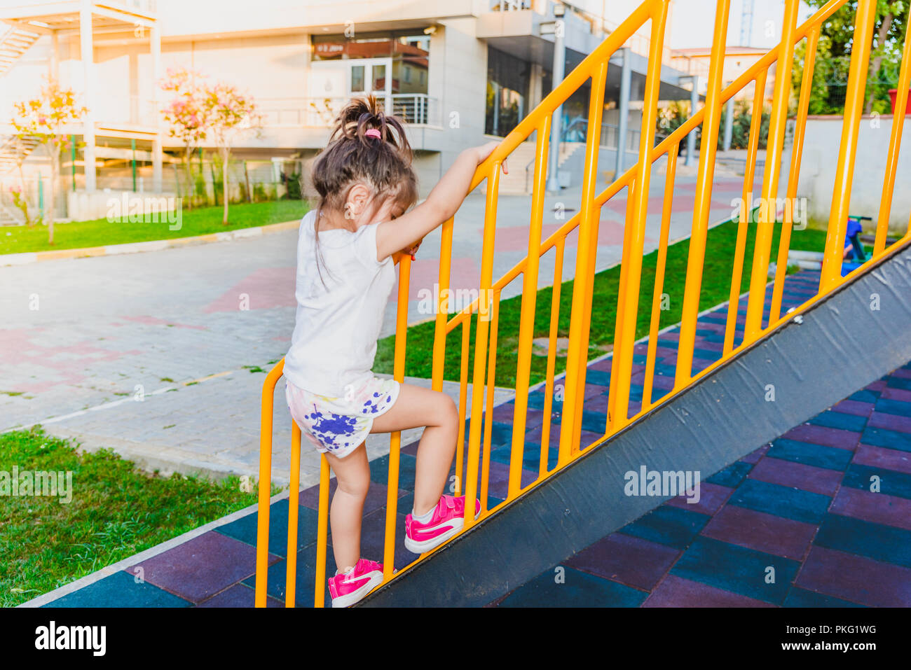 Back side view of cute little girl tying to climb from metallic stairs ...