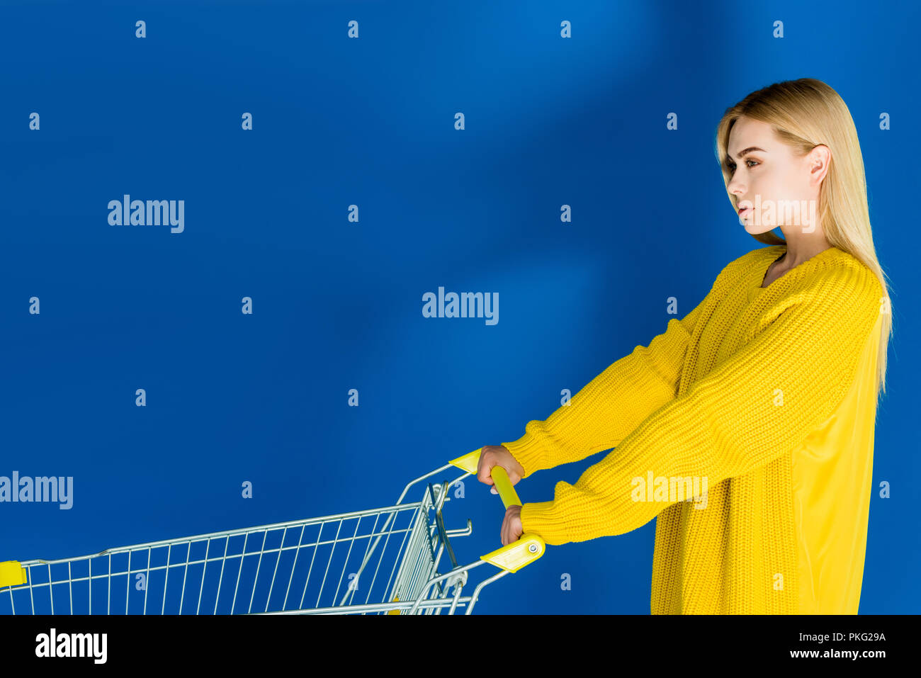 Attractive young girl pushing shopping cart on blue background Stock ...