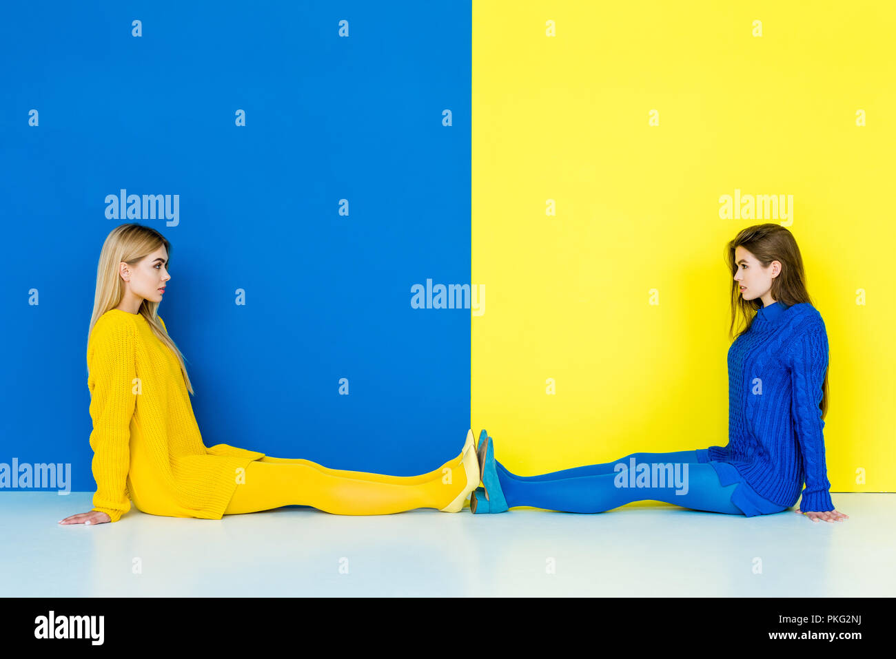 Female fashion models sitting on floor towards each other on blue and ...