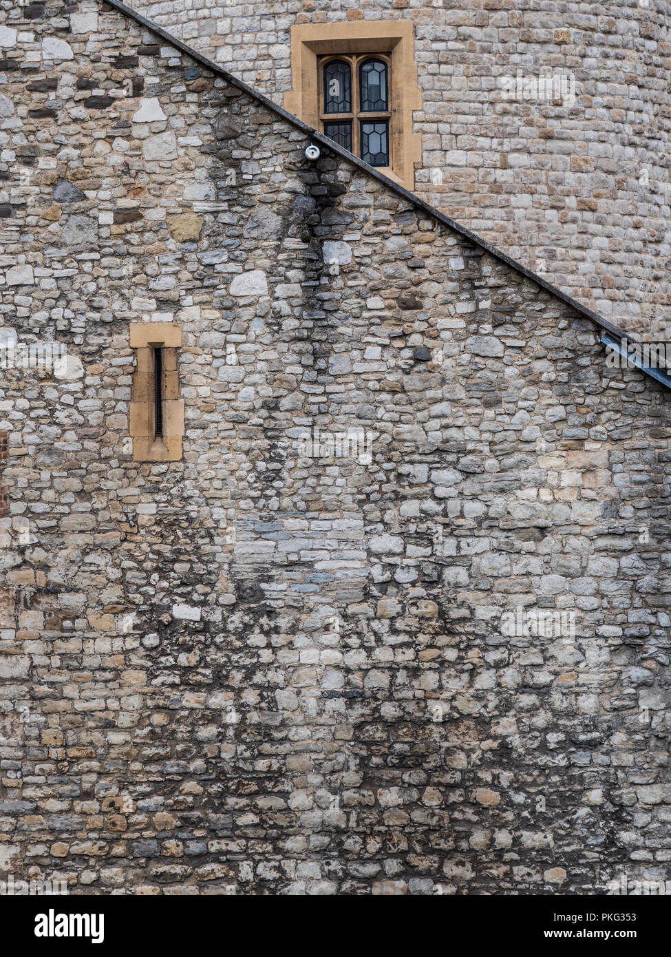A view of a very old stone wall with a narrow window and angled roof ...