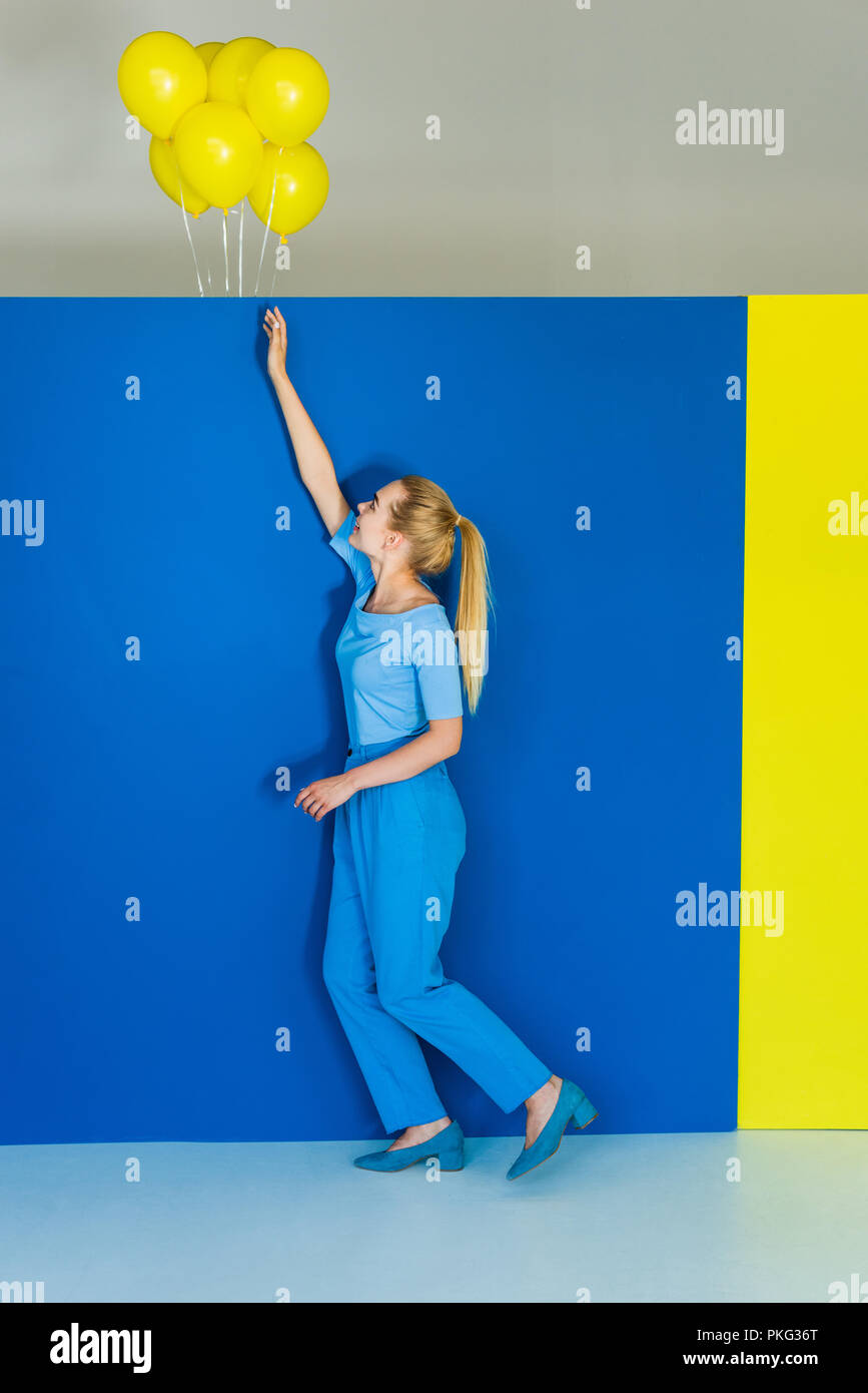 Beautiful blonde girl reaching out for yellow balloons on blue and ...