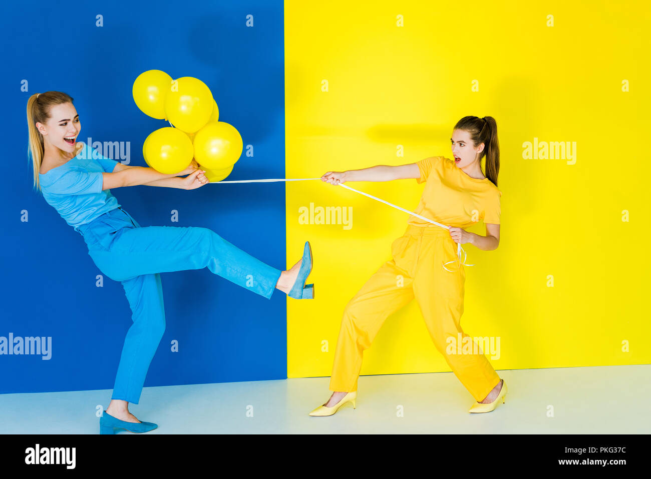 Blonde and brunette girls fighting for balloons on blue and yellow ...