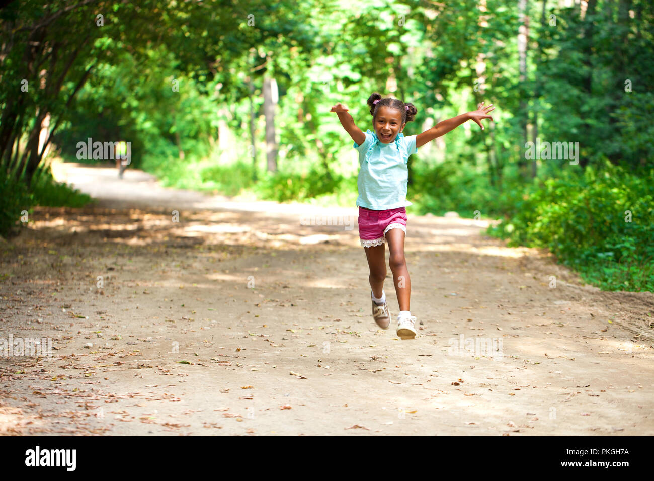 Portrait of smiling african american little girl running in summer park ...