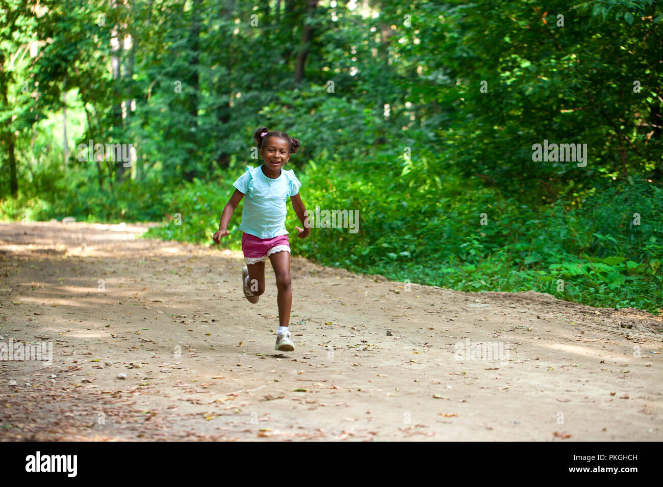 Portrait of smiling african american little girl running in summer park ...
