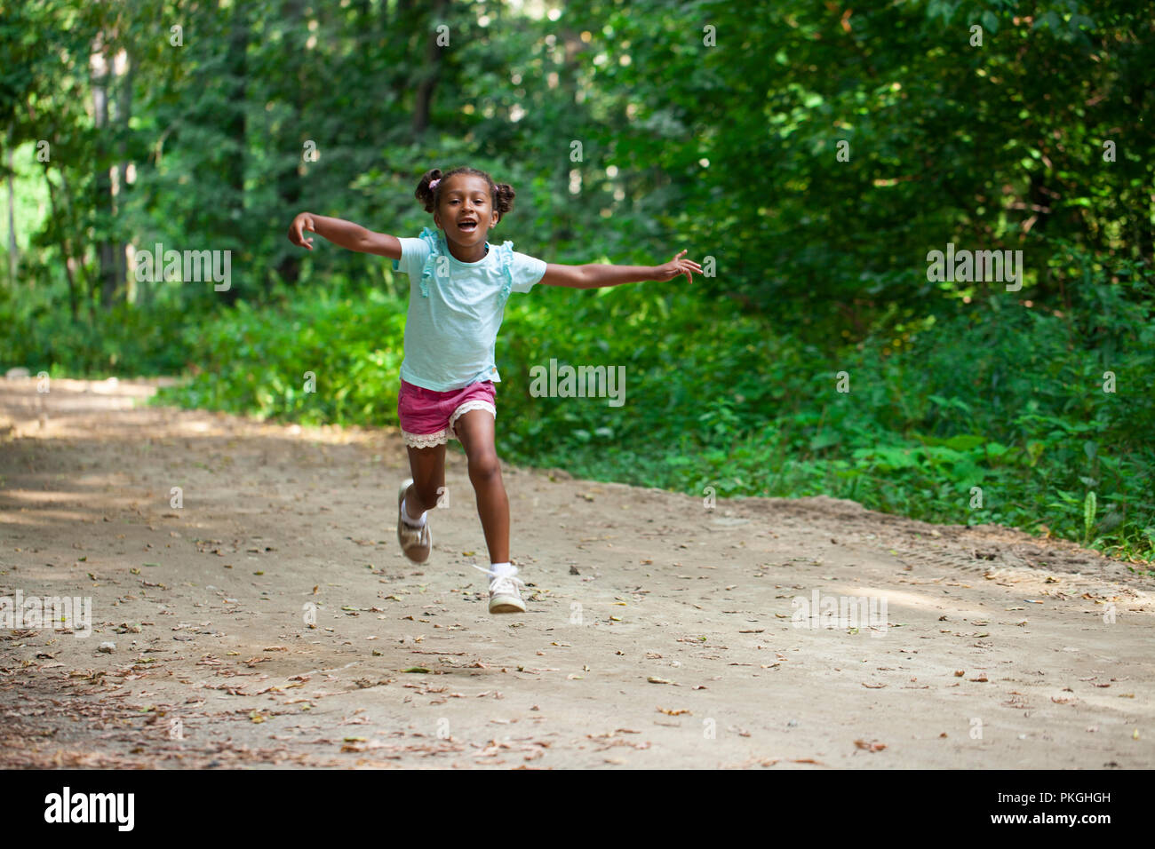 Portrait of smiling african american little girl running in summer park ...