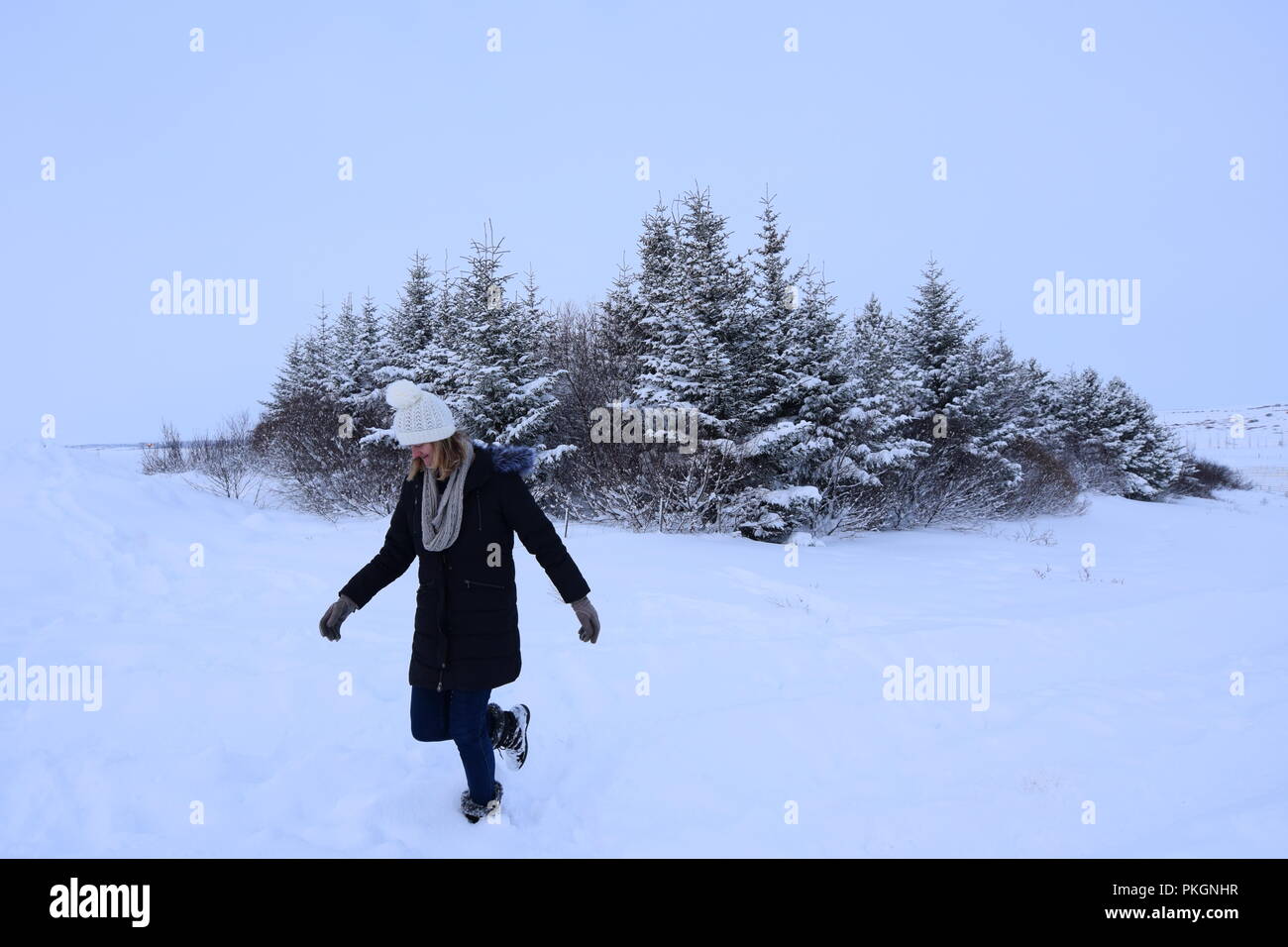 Woman seeing snow for the first time kicking snow in field with trees ...