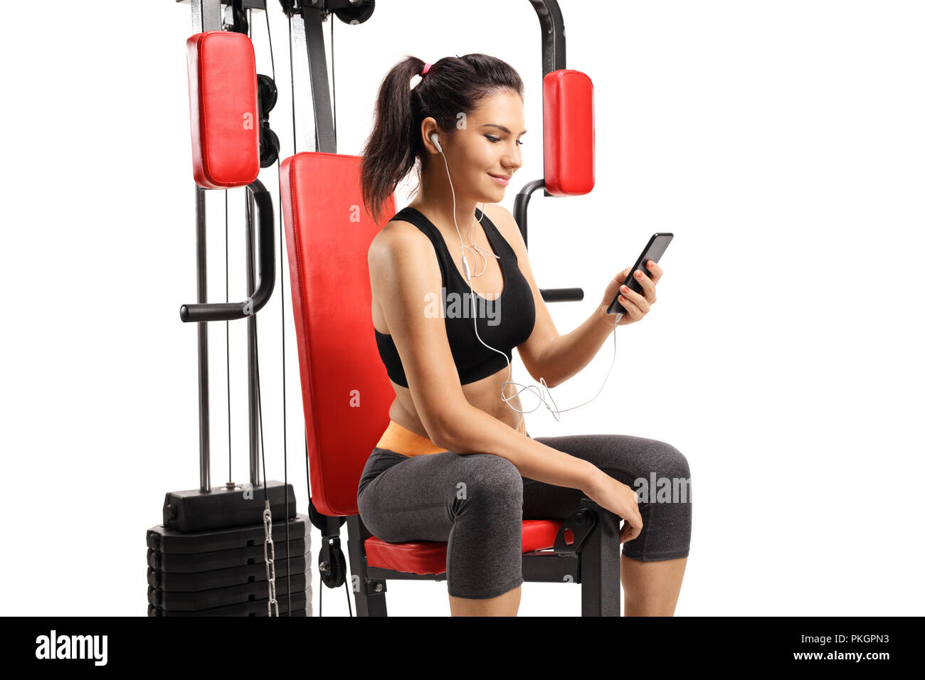 Young female with a cell phone sitting on an exercise machine isolated ...