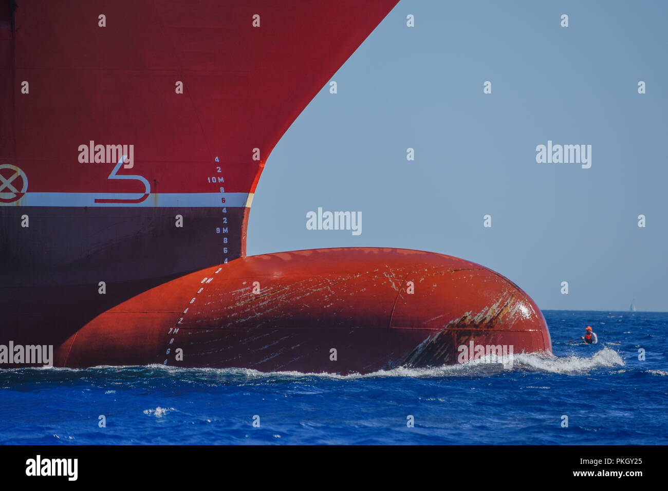 The bulbous bow of a large cargo ship looms over a tiny kayaker Stock ...