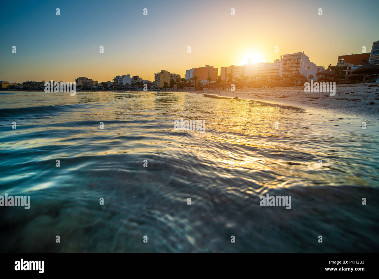Golden waves of the sea and city on horizon during sunset Stock Photo ...
