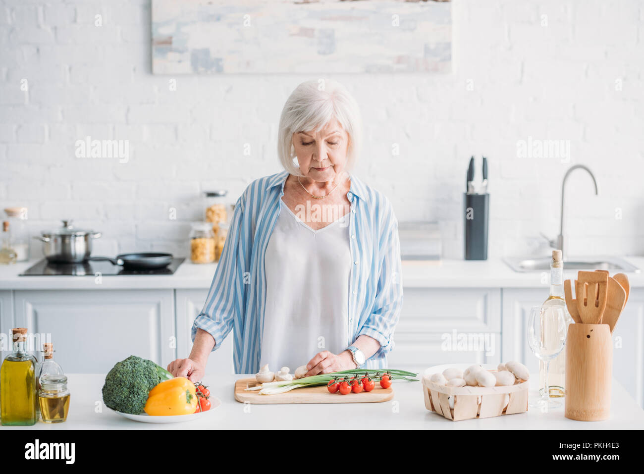 portrait of senior lady cutting vegetables while cooking dinner at ...