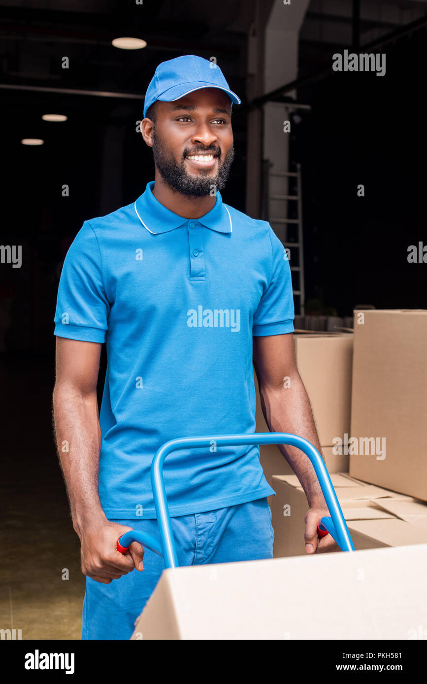 smiling african american delivery man holding cart with boxes Stock ...