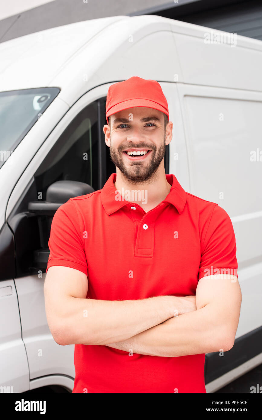 smiling caucasian delivery man standing with crossed arms and looking ...