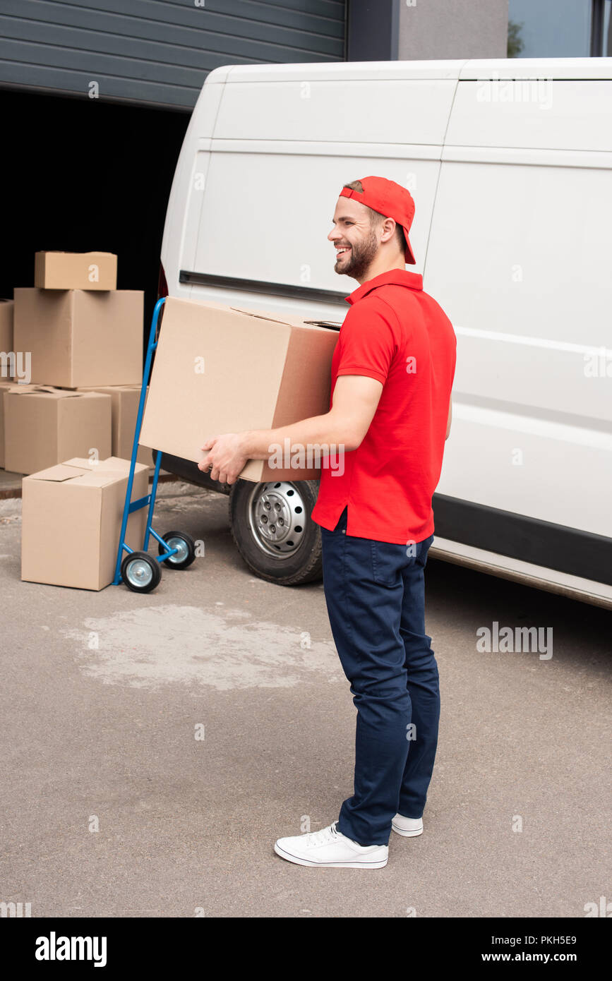 side view of young delivery man in uniform with cardboard box standing ...
