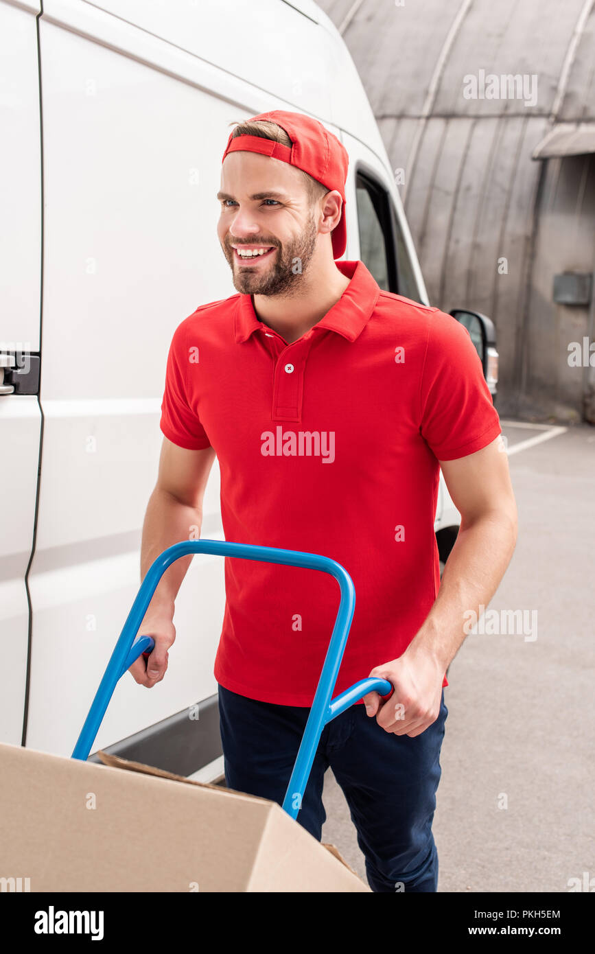 smiling delivery man with cardboard box on delivery cart Stock Photo ...