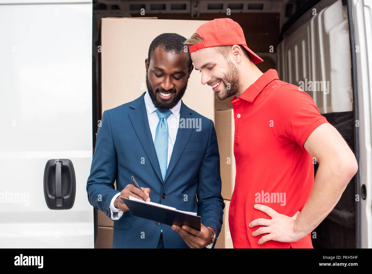 portrait of smiling multicultural businessman and delivery man looking ...