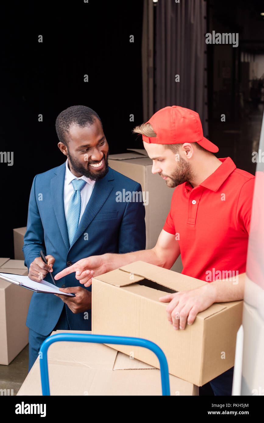 portrait of multicultural businessman and delivery man discussing order ...