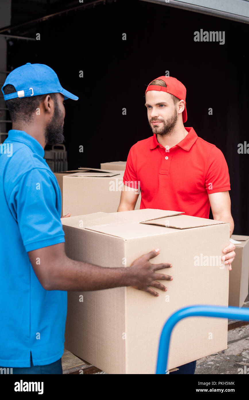 multicultural delivery men in red and blue uniform with cardboard boxes ...