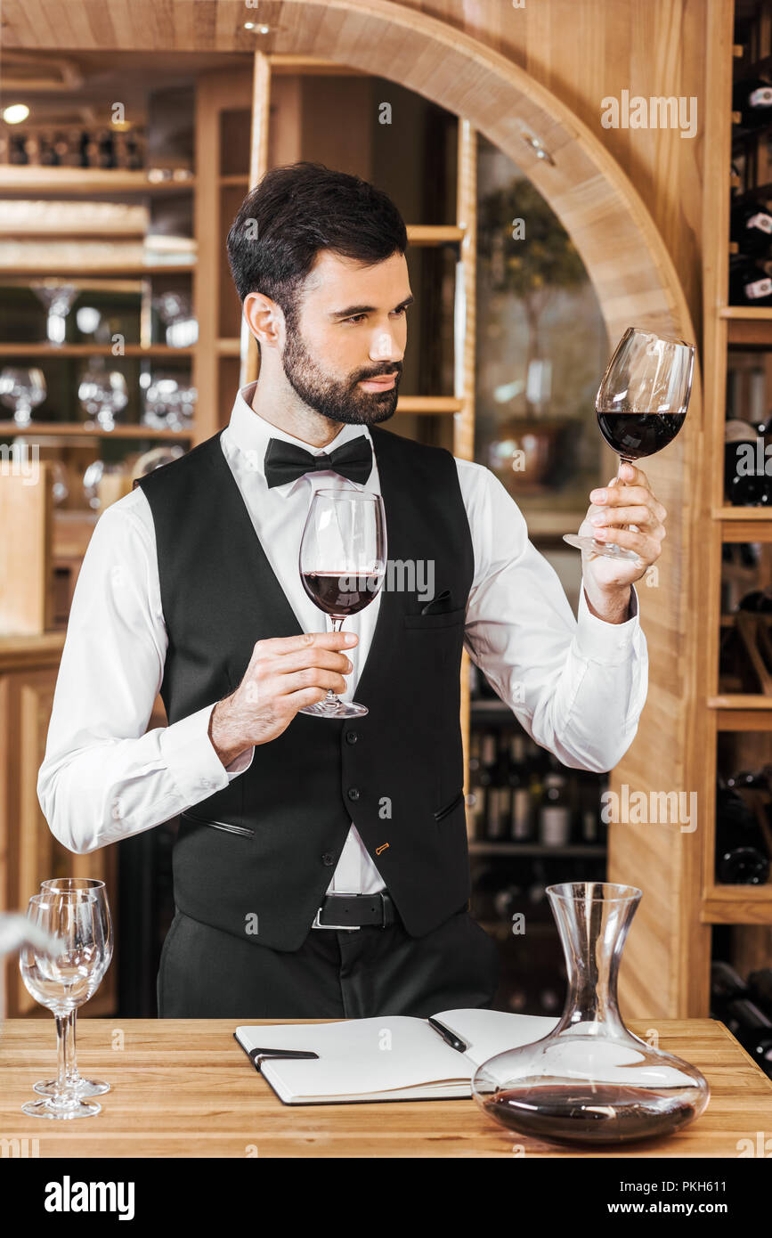 confident young sommelier examining color of wine at wine store Stock ...