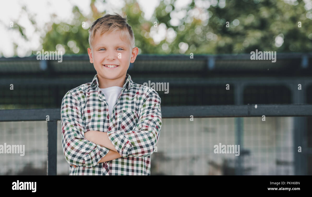 happy boy in checkered shirt standing with crossed arms and smiling at ...