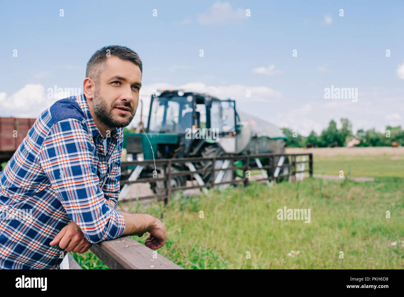 pensive middle aged farmer leaning at railing and looking away at farm ...