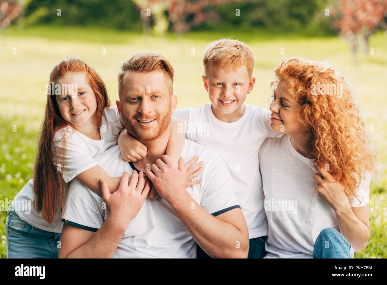 beautiful happy redhead family hugging and smiling at camera in park ...