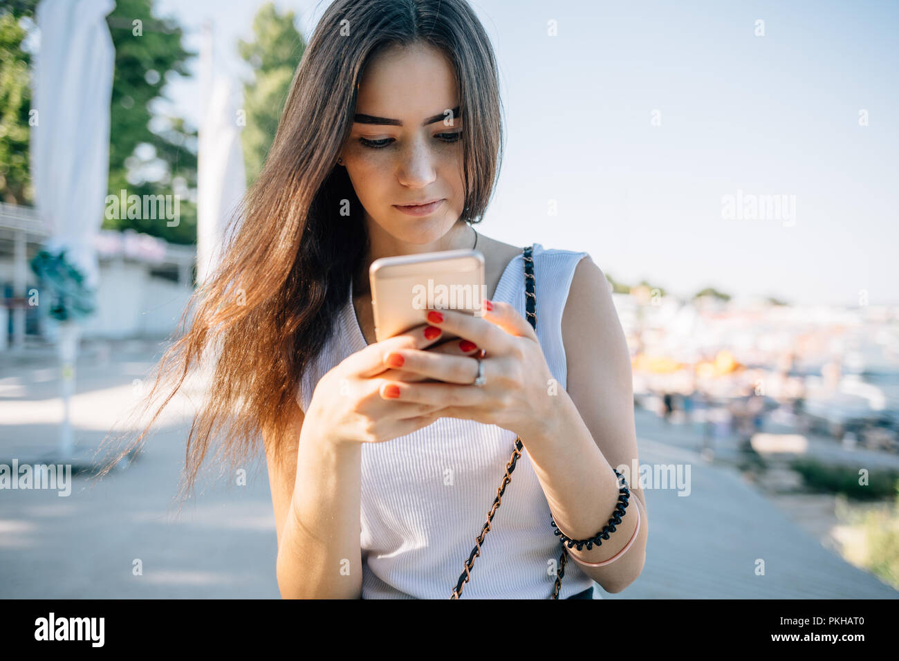 Portrait of young woman with long brown hair standing texting outside ...