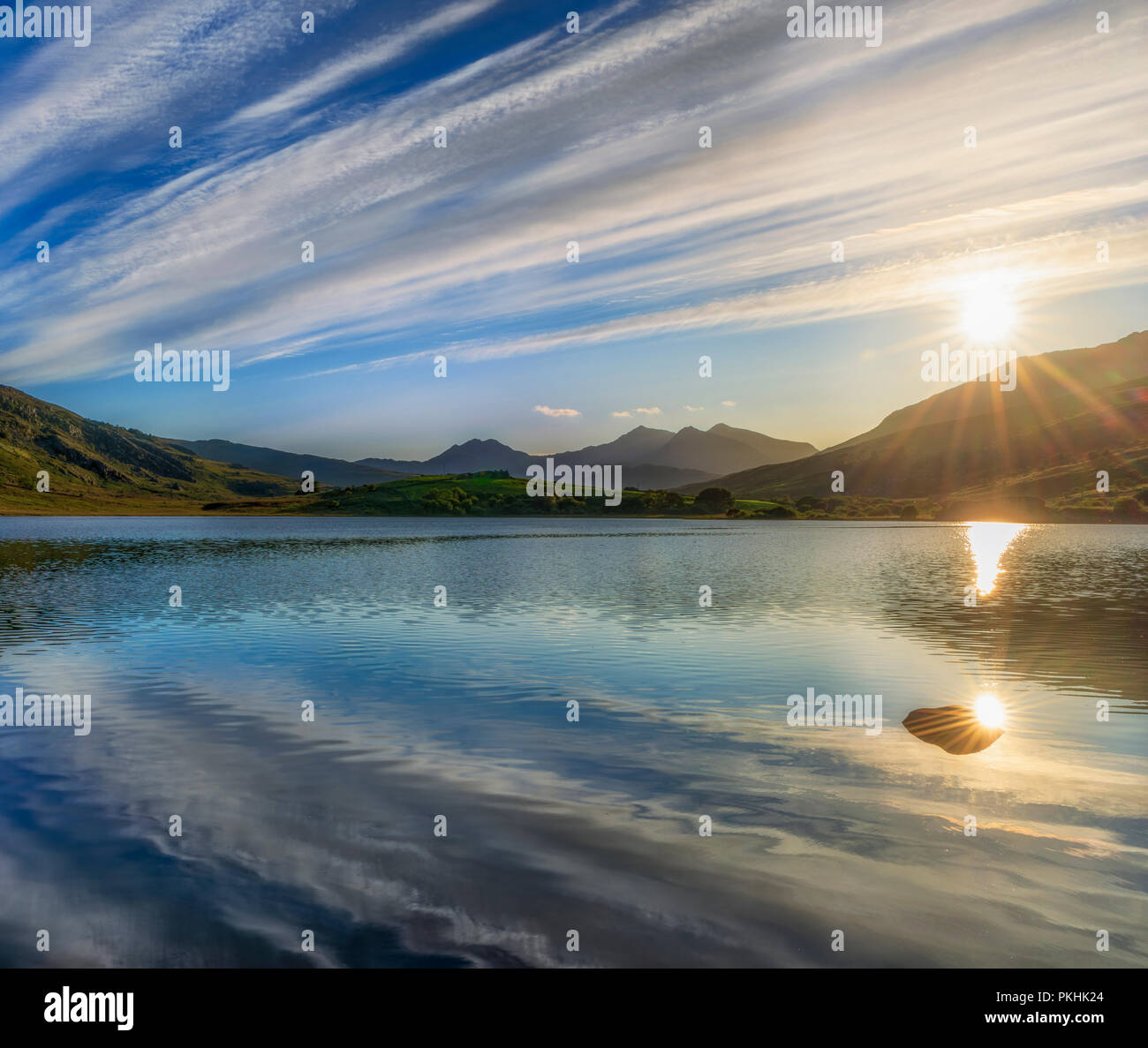 The lake Llynnau Mymbyr reflecting the blue sky, clouds and sun with ...