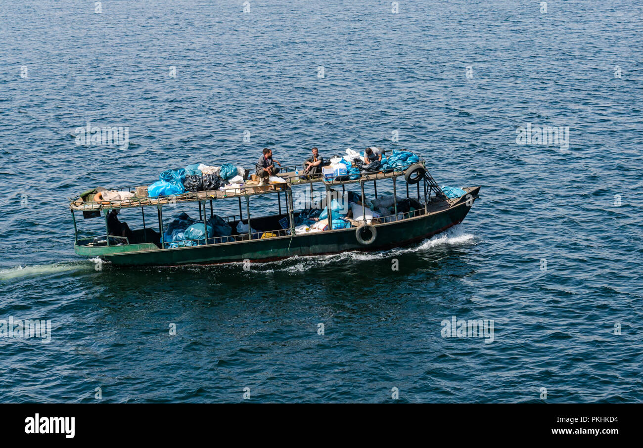 River boat transporting waste rubbish with men sitting on top of roof ...