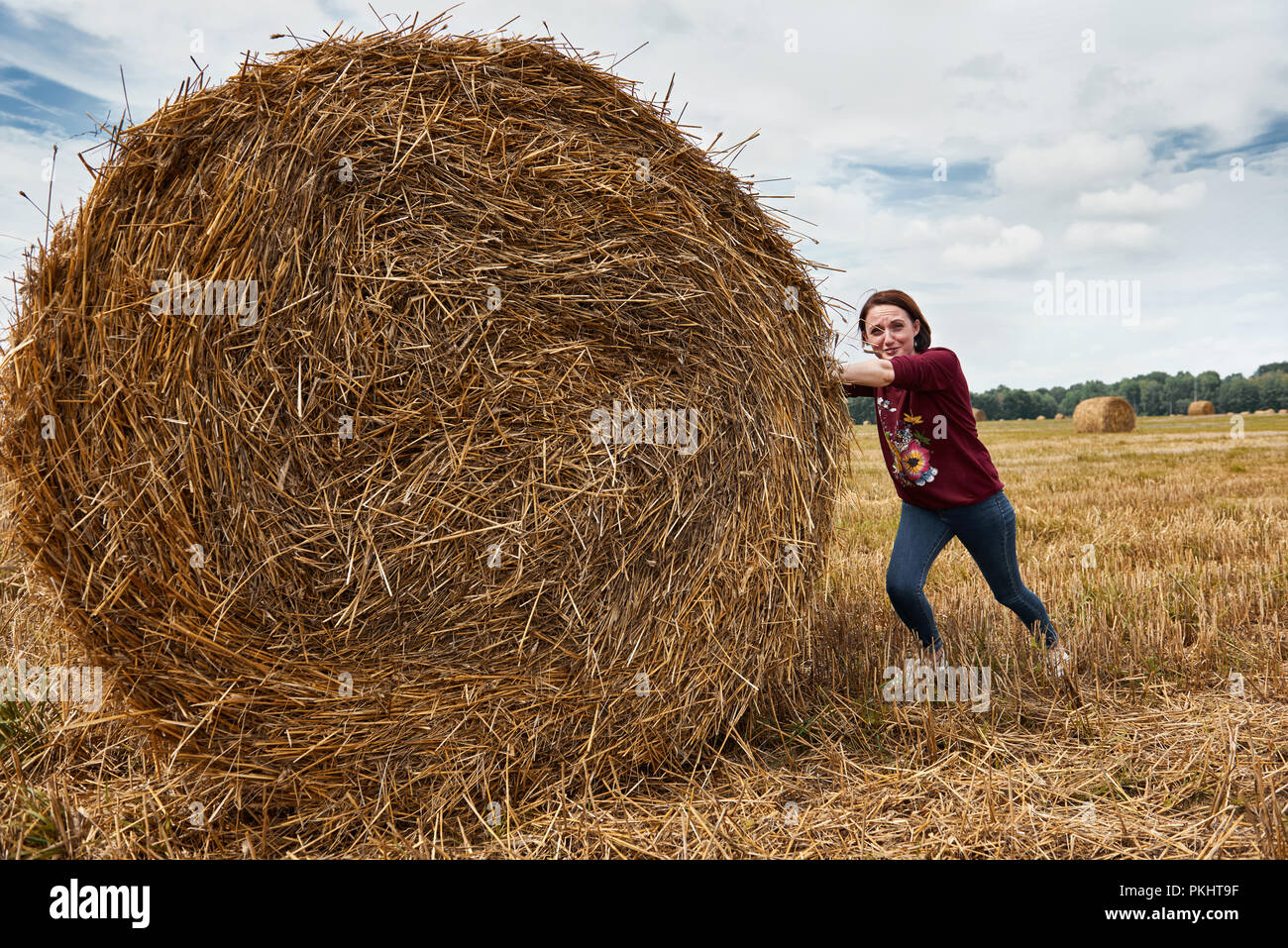 young girl having fun in the field, pushes the haystack Stock Photo - Alamy
