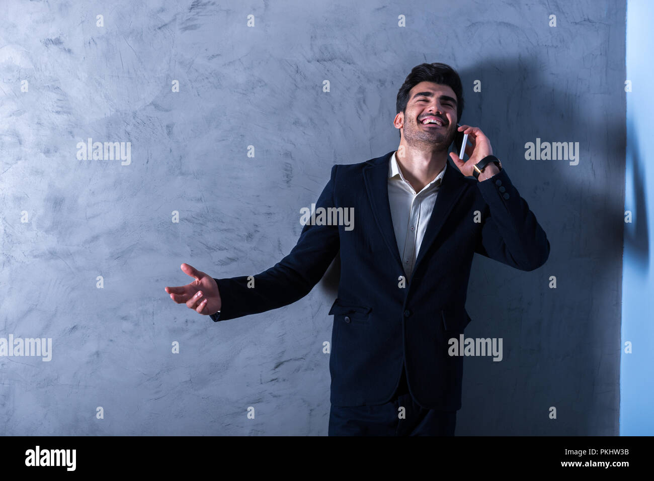 A happy handsome young businessman in a black suit talking on his phone ...