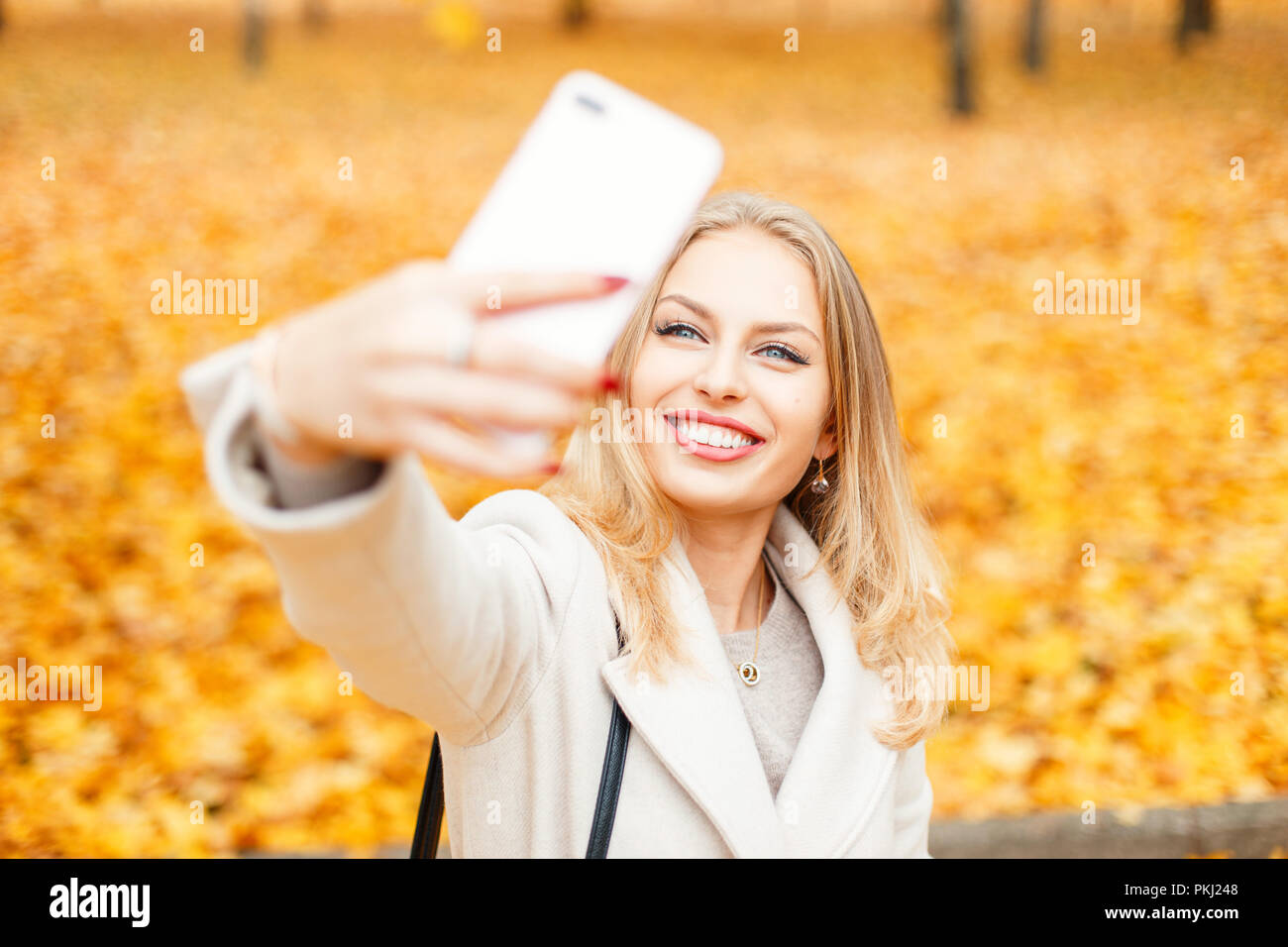 Happy girl with a smile doing selfie in a fall day against a background ...