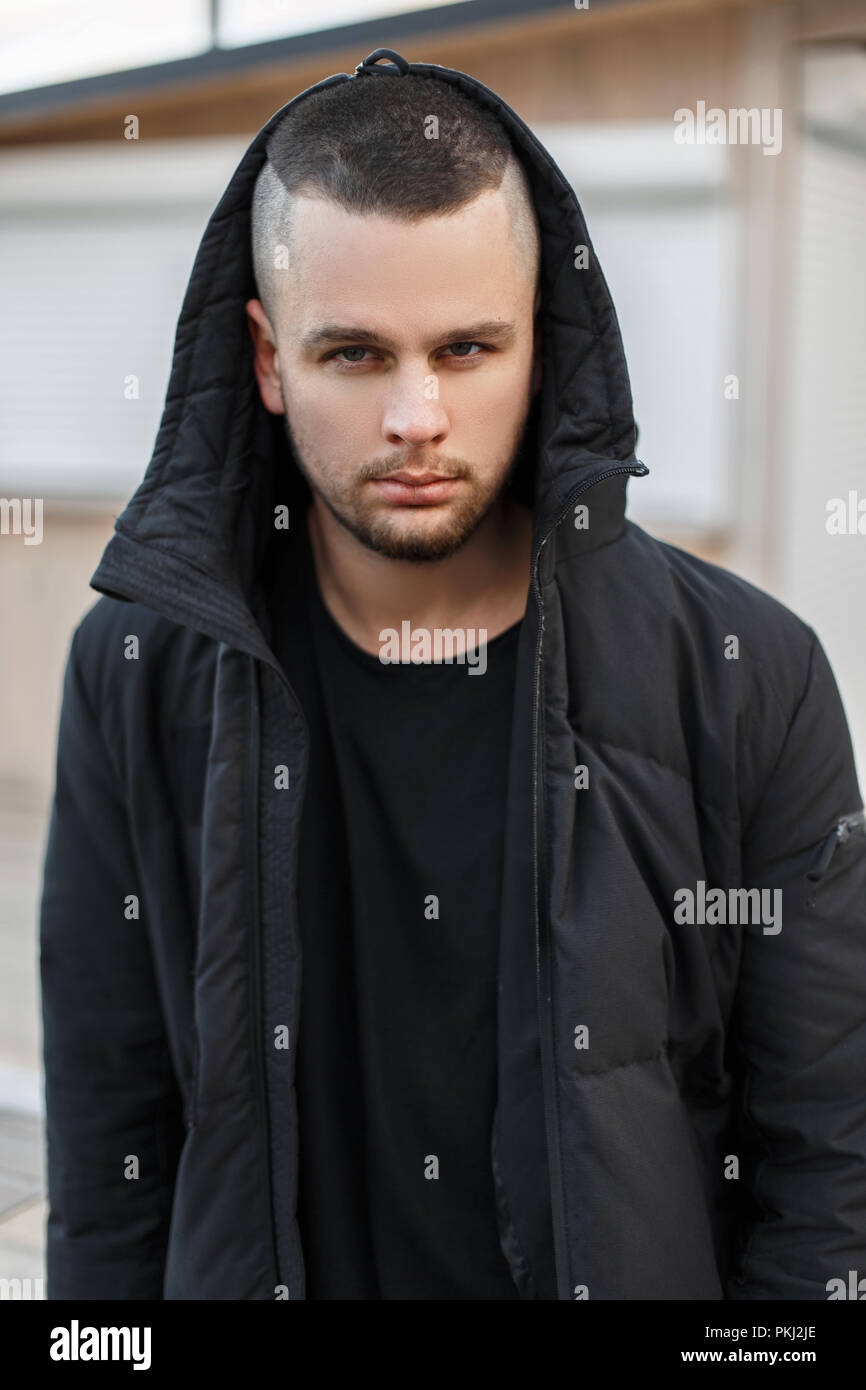 Stylish beautiful young man with a hood in a black winter jacket on the ...