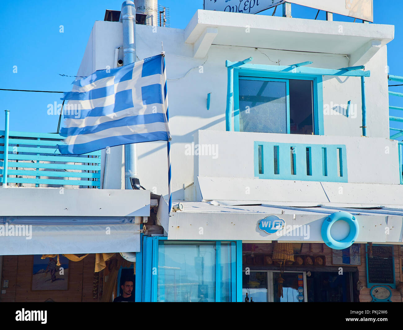 A typical blue balcony of a Greek tavern with a flag waving on a blue ...