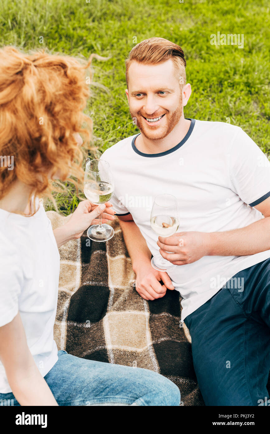 high angle view of happy rdhead couple drinking wine at picnic in park ...