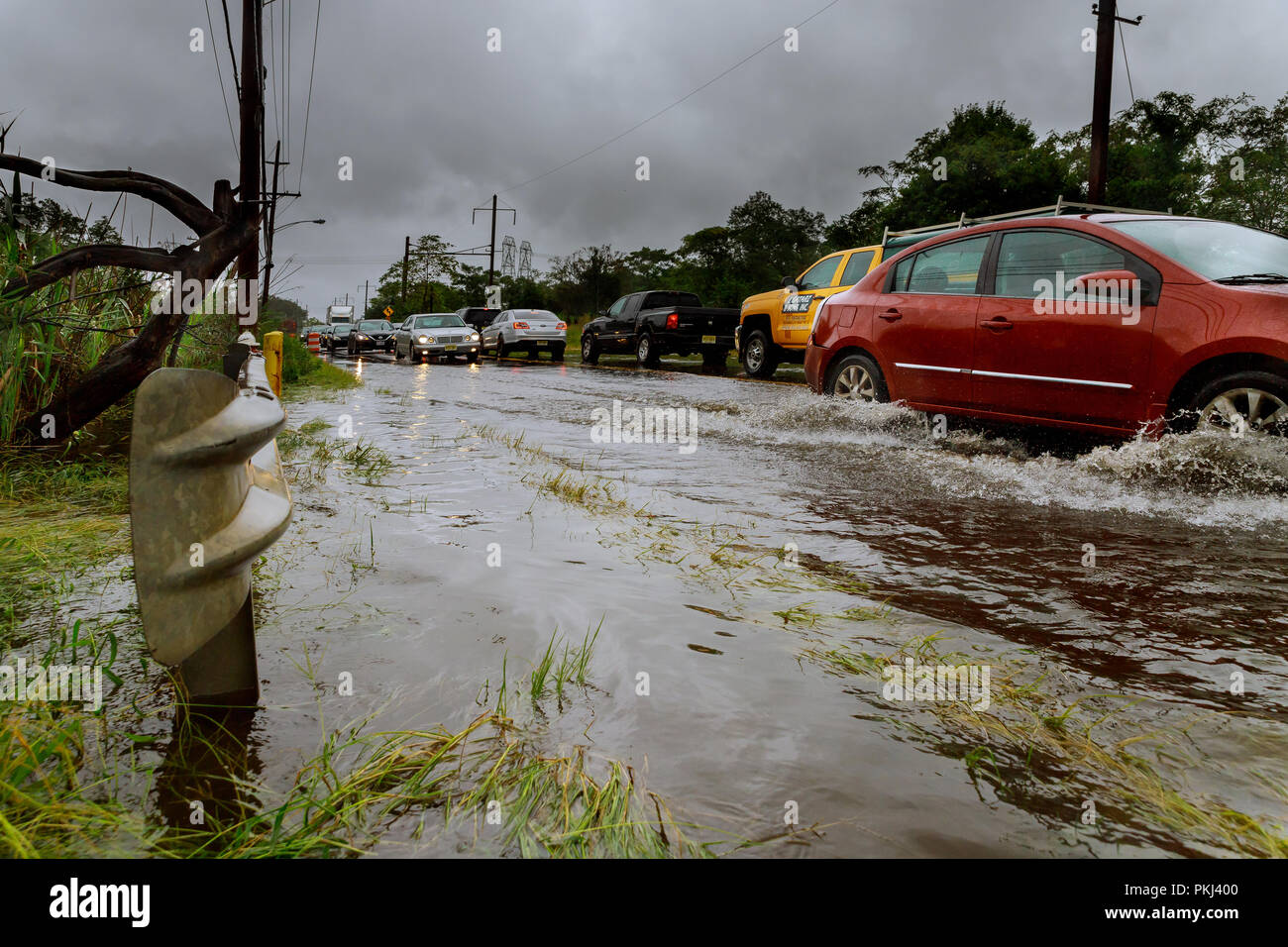 A line of cars ride on a road under water. Flood on the street splash ...