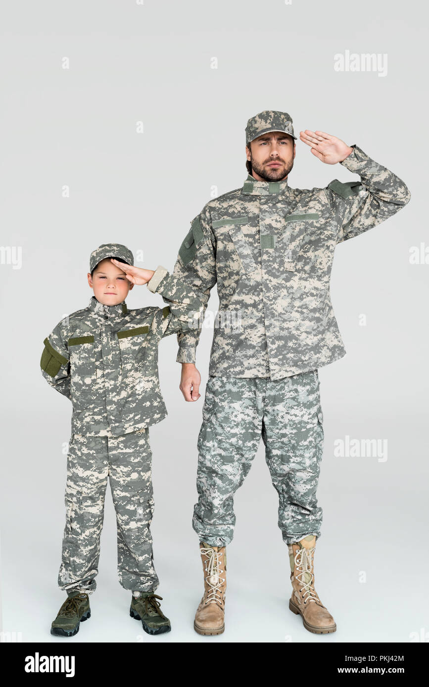 father and son in military uniforms saluting and looking at camera on ...