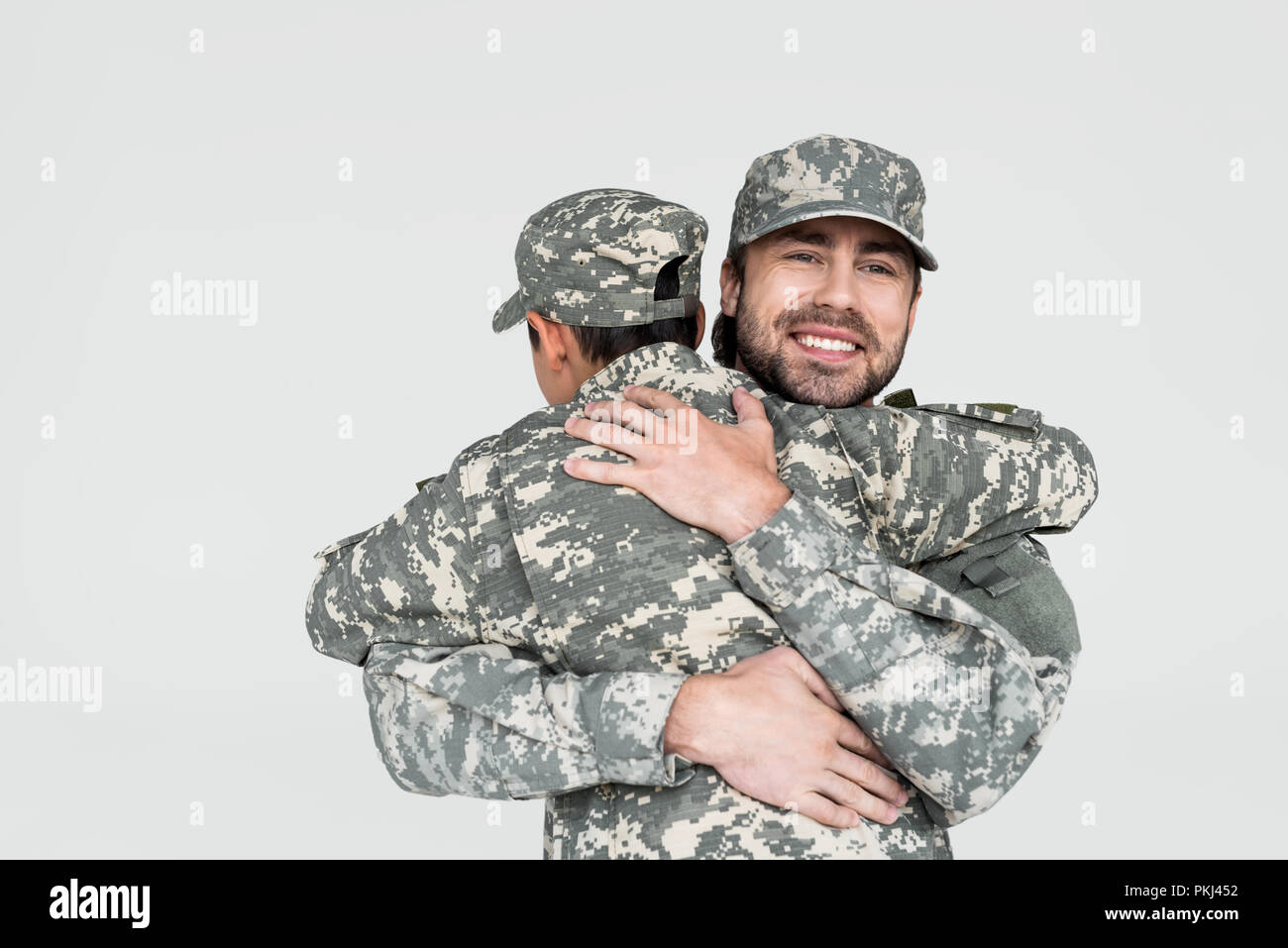 partial view of smiling soldier and son in military uniforms hugging ...