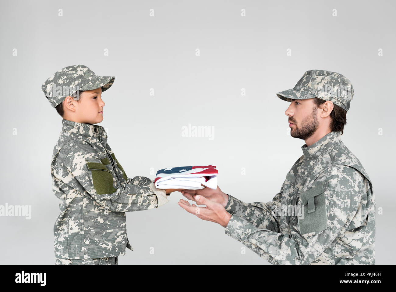 side view of little boy in camouflage clothing giving folded american ...