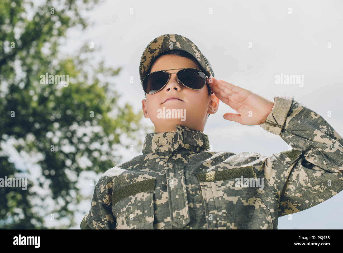 portrait of little boy in camouflage clothing and sunglasses saluting ...