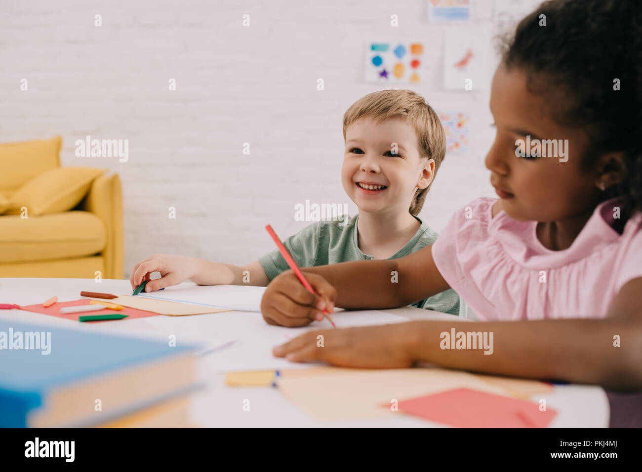 selective focus of multicultural preschoolers at table with papers and ...