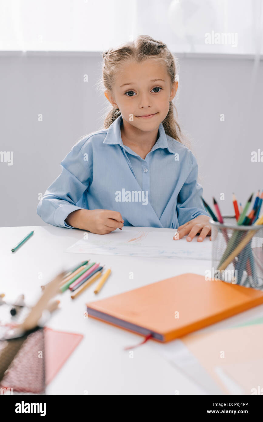 portrait of smiling kid sitting at table with colorful pencils and ...