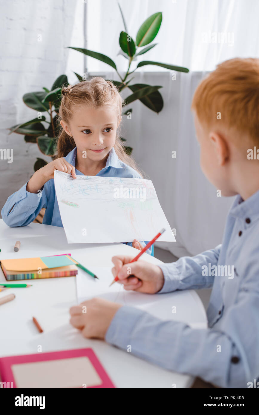 selective focus of adorable kids drawing pictures at table in classroom ...