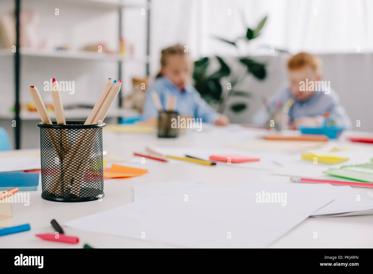 selective focus of adorable kids drawing pictures at table in classroom ...