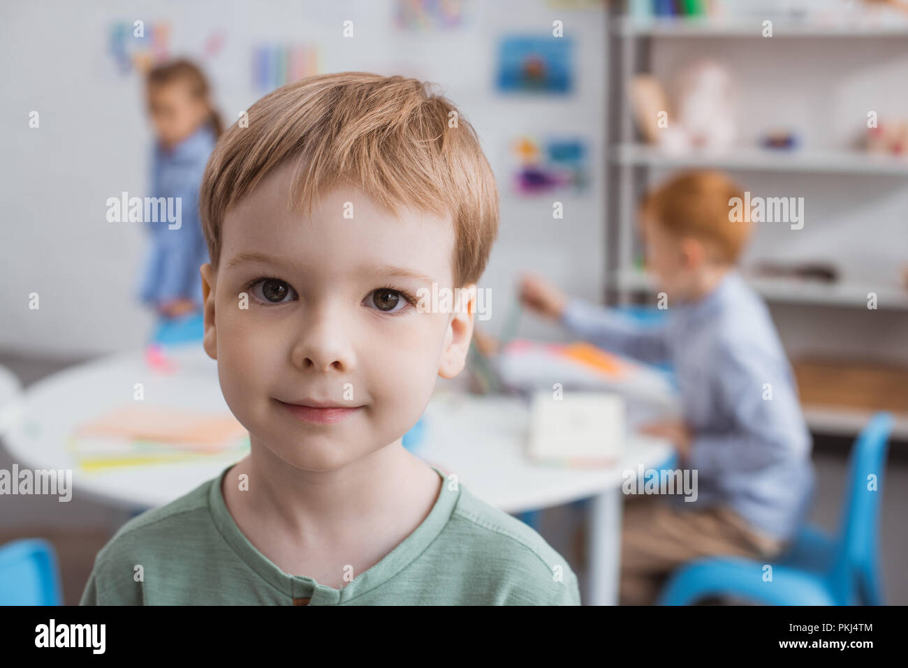 selective focus of cute little boy looking at camera with classmates ...