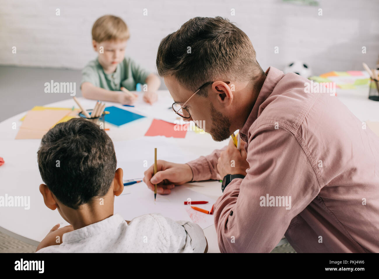 selective focus of teacher and multiracial boys drawing pictures with ...