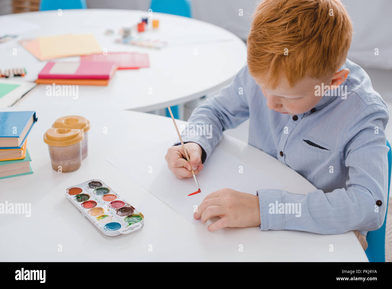 focused preschooler red hair boy drawing picture at table in classroom ...