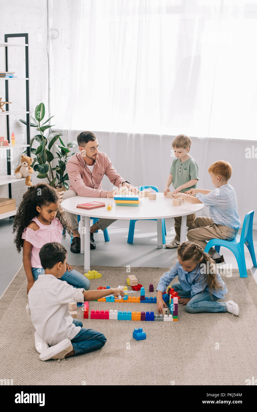 teacher and multicultural preschoolers on floor with colorful bricks in ...