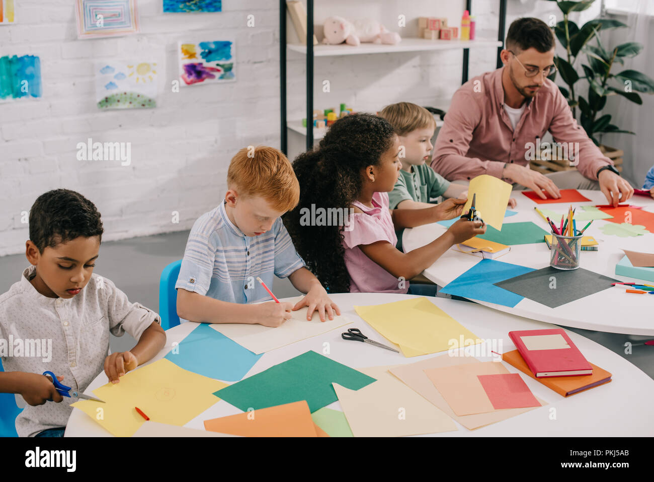 teacher and multicultural preschoolers cutting colorful papers with ...